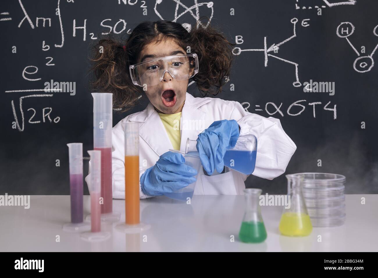 funny scientist girl with gloves and goggles in lab coat mixing ...