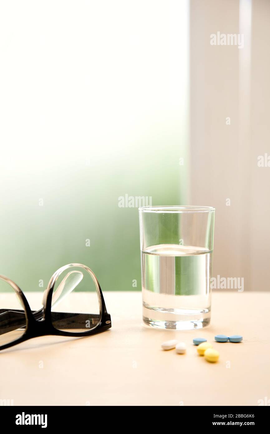 Medication next to a pair of glasses and a glass of water Stock Photo ...