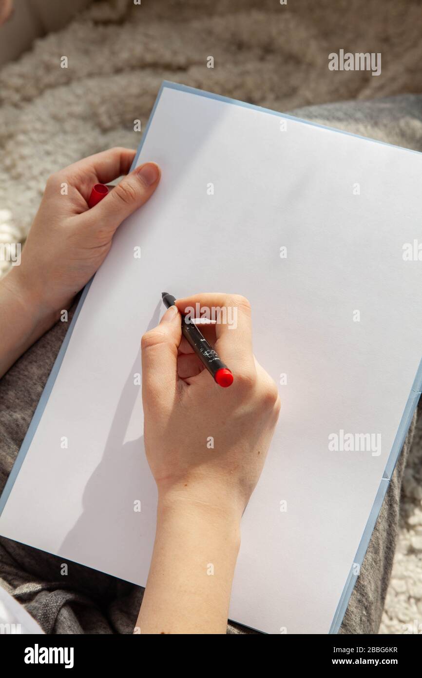 a girl at home alone draws on a sheet of paper. Close up of hands ...