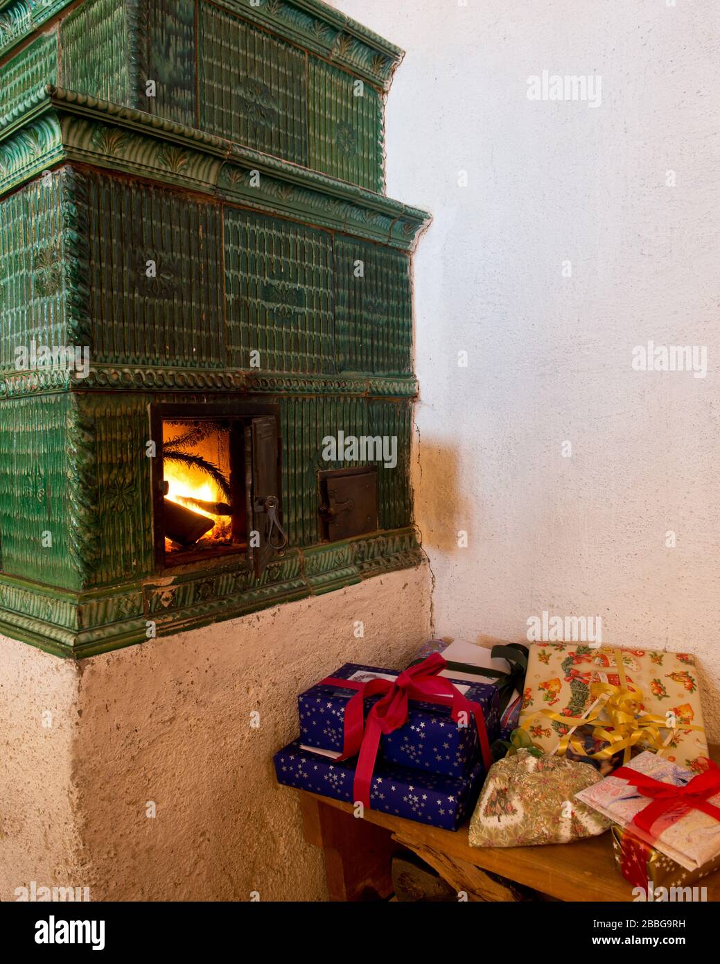 green tiled stove with log fire and wrapped Christmas parcels Stock ...