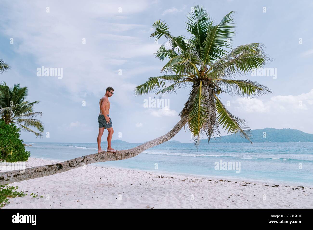 La Digue Seychelles, young men walking at the white beach with clear ...