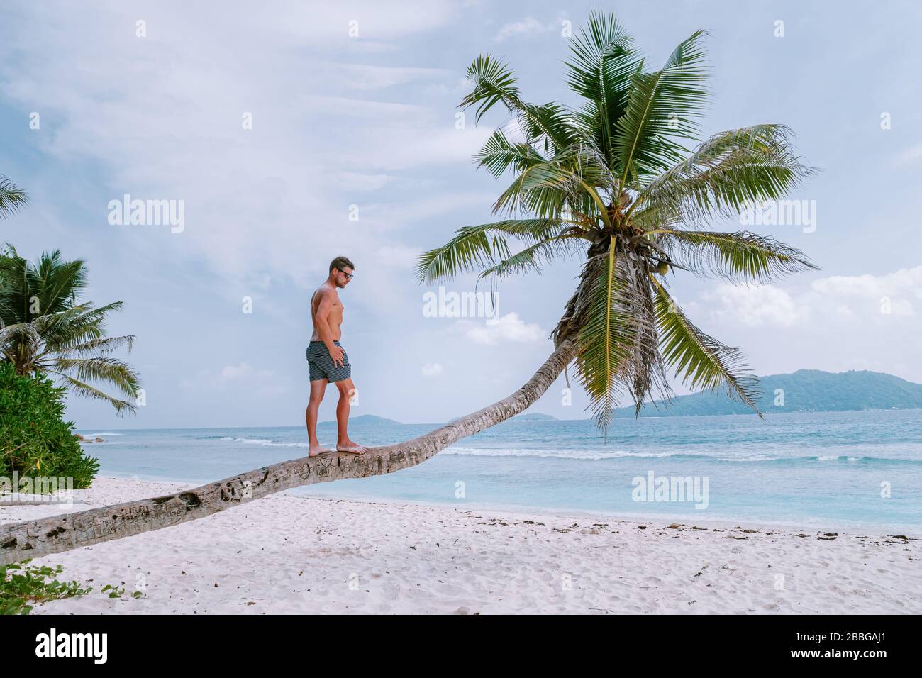 La Digue Seychelles, young men walking at the white beach with clear ...