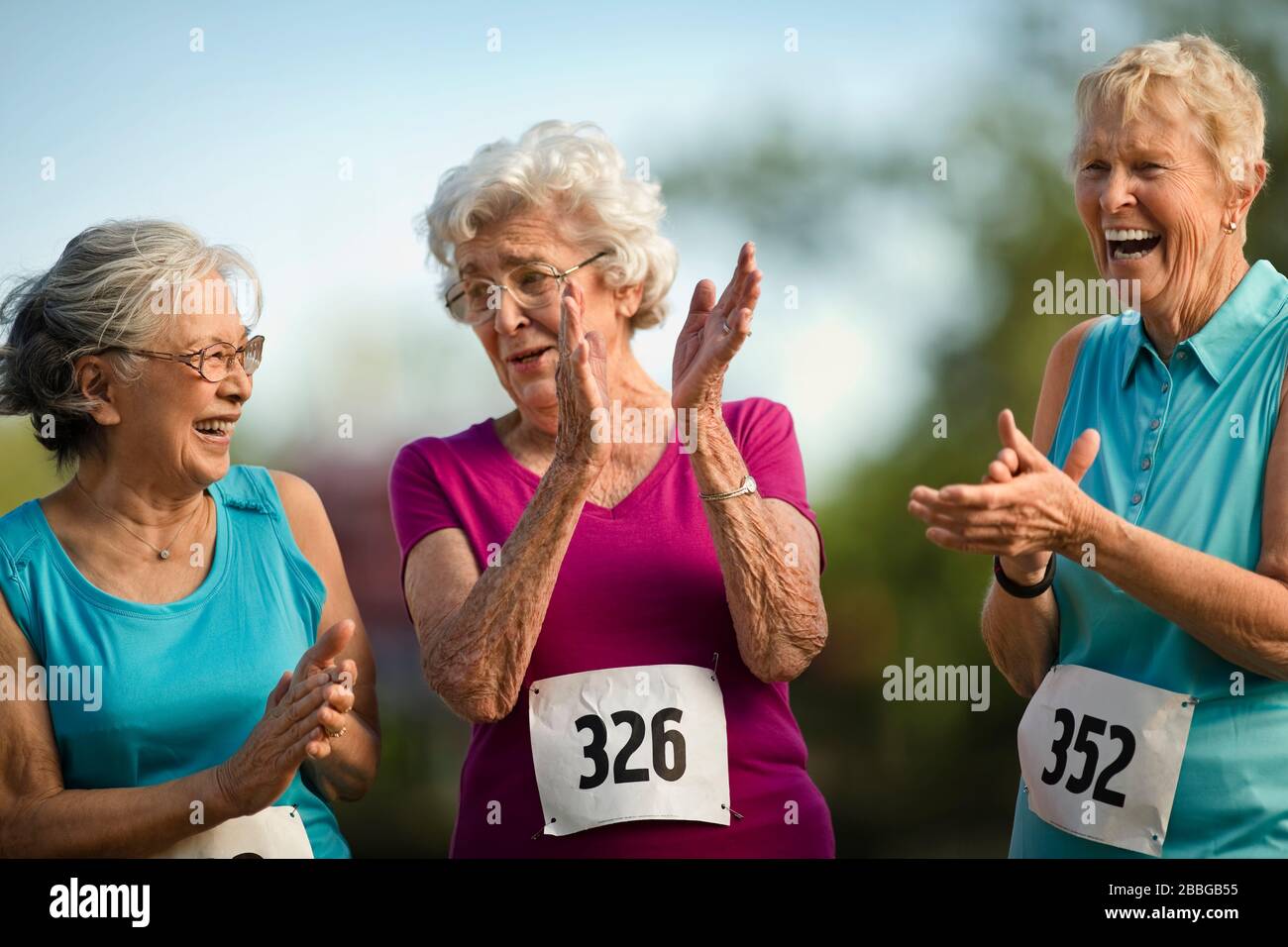 Three smiling senior women clapping and laughing during an athletics ...