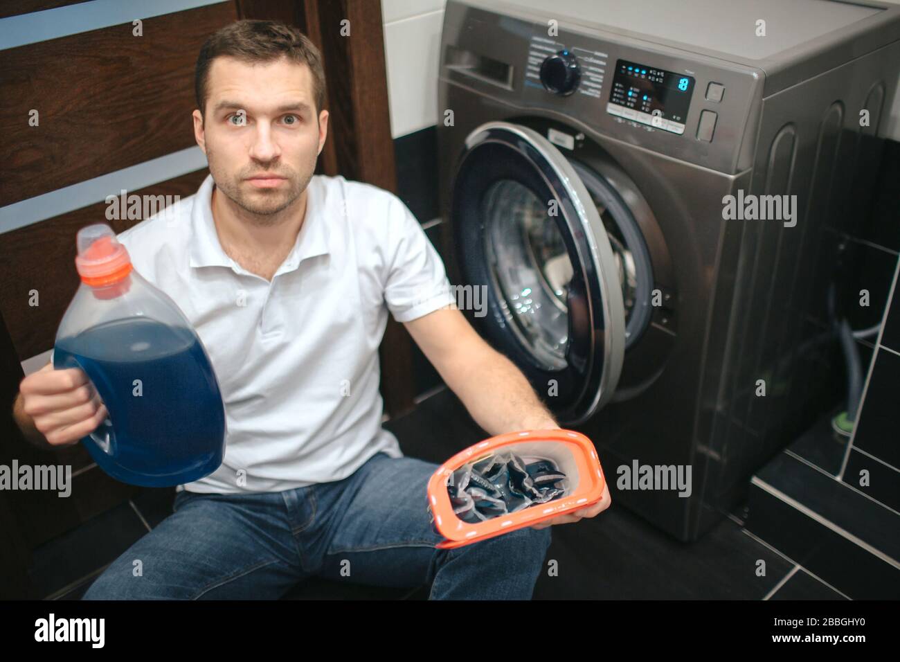 Serious concentrated guy in bathtub hold liquid powder and look on ...