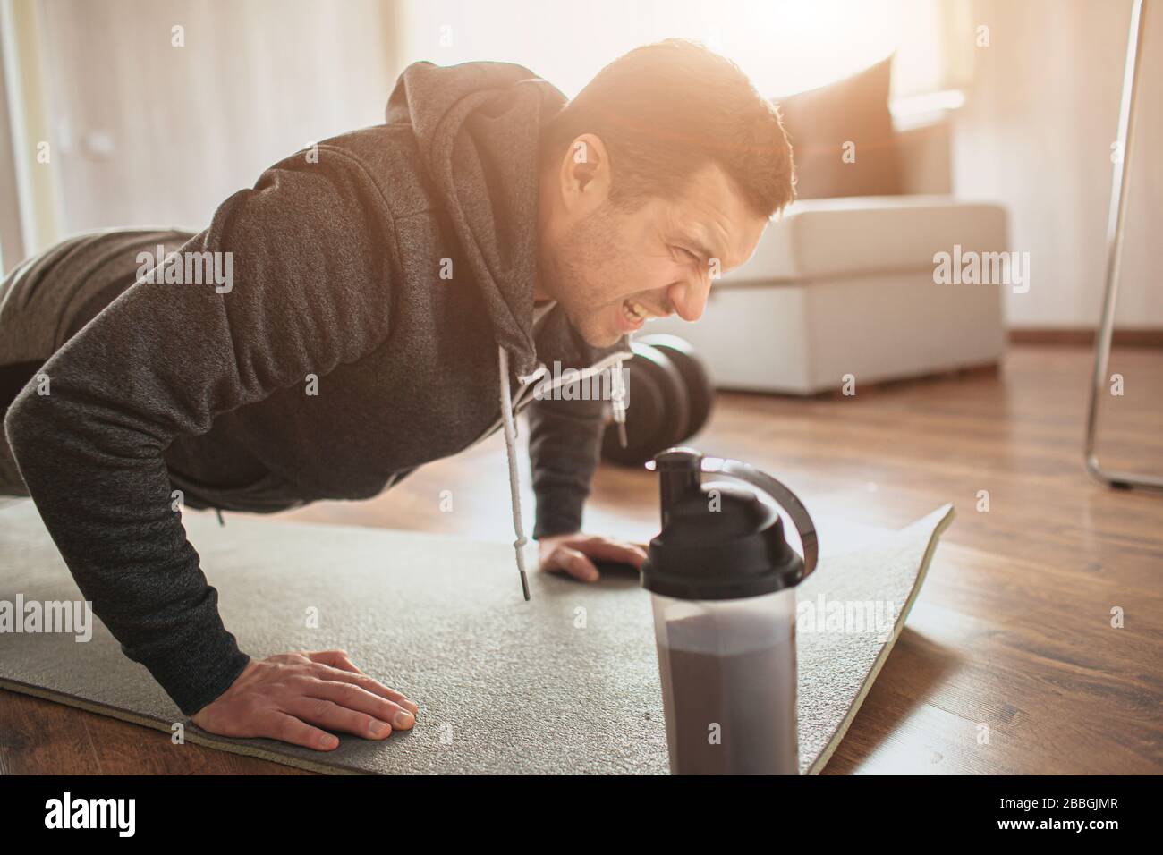 Young ordinary man go in for sport at home. Wink and scream because of ...