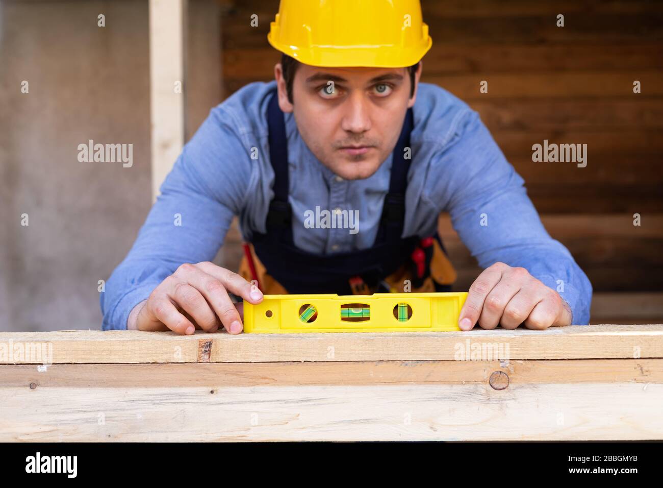 Portrait of a handsome young carpenter measuring lumber with spirit ...