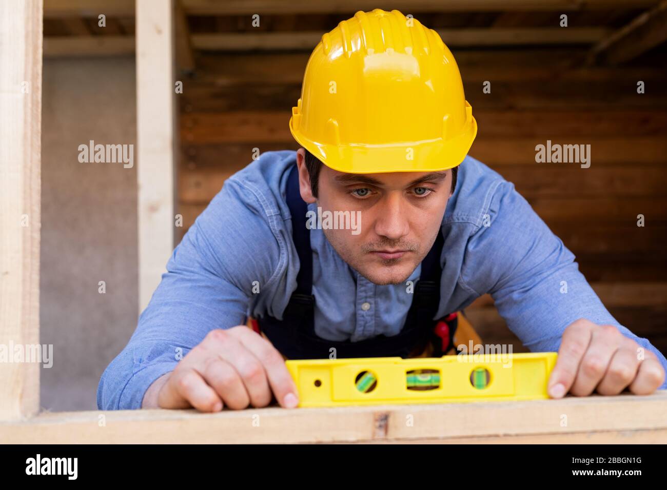 Portrait of a handsome young carpenter measuring lumber with spirit ...