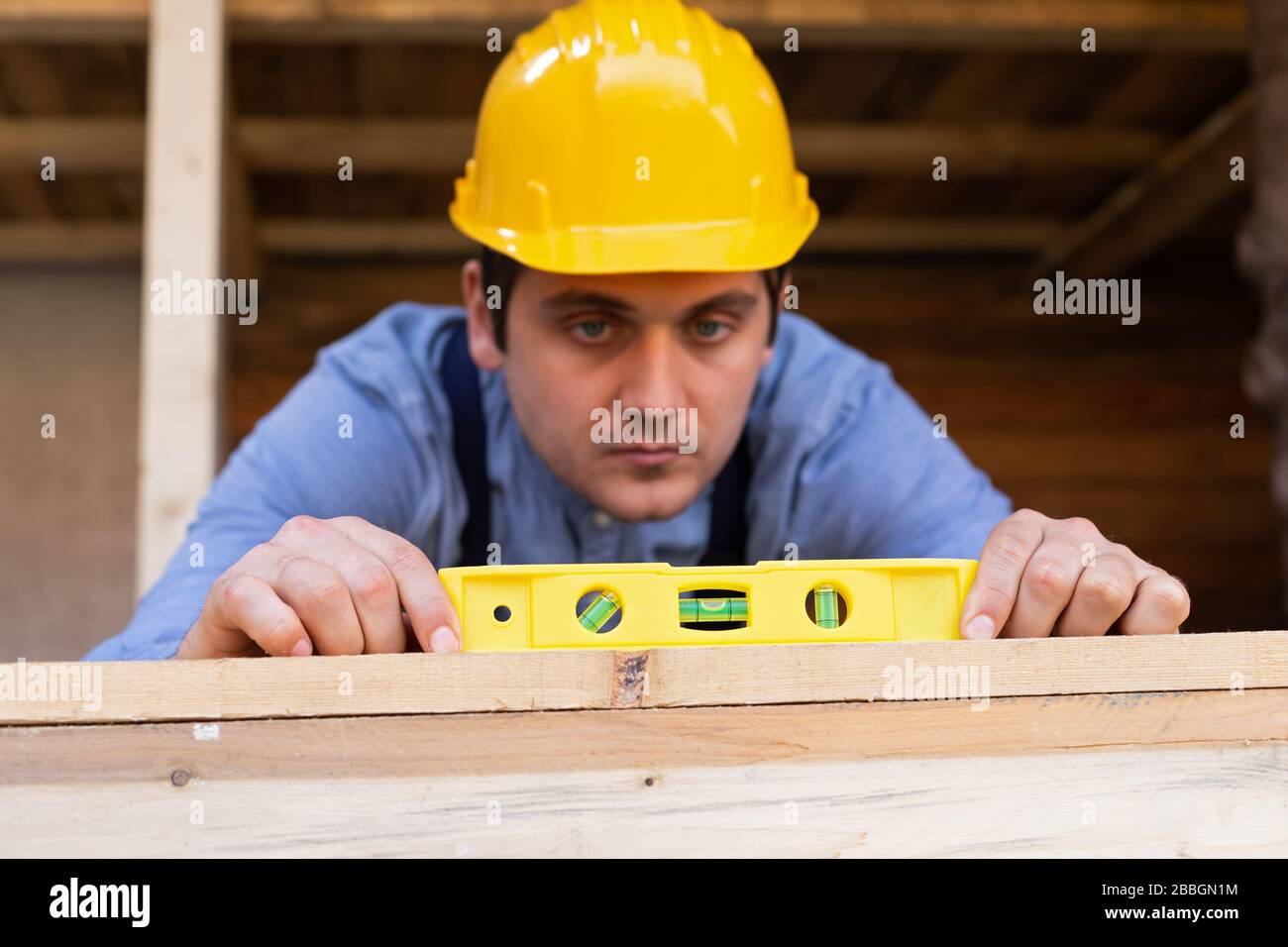 Portrait of a handsome young carpenter measuring lumber with spirit ...