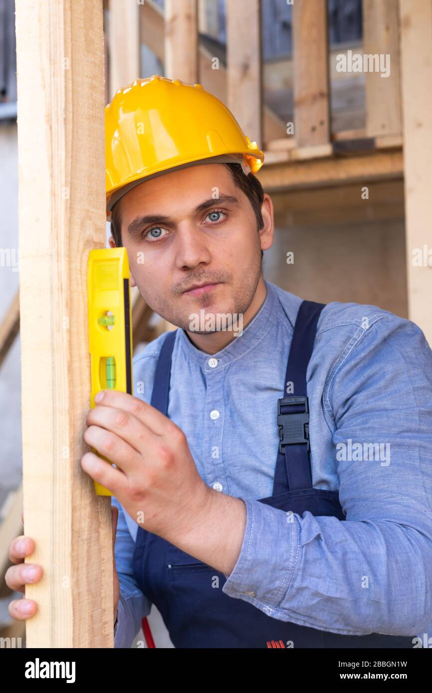 Portrait of a handsome young carpenter measuring lumber with spirit ...