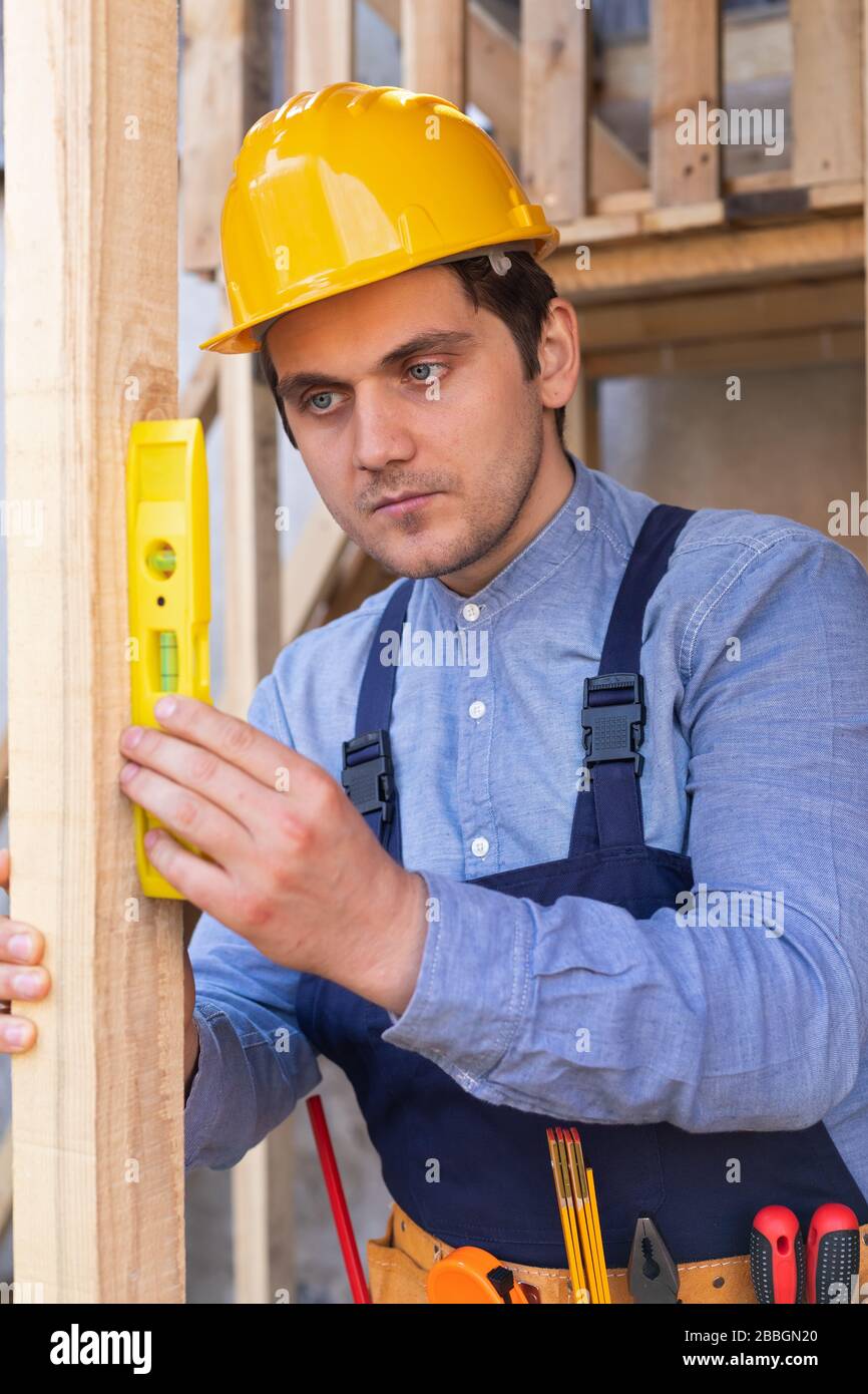 Portrait of a handsome young carpenter measuring lumber with spirit ...