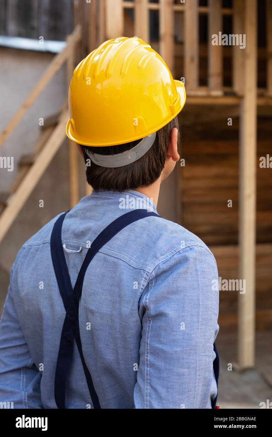 Back view of young carpenter with yellow hard hat and blue shirt ...