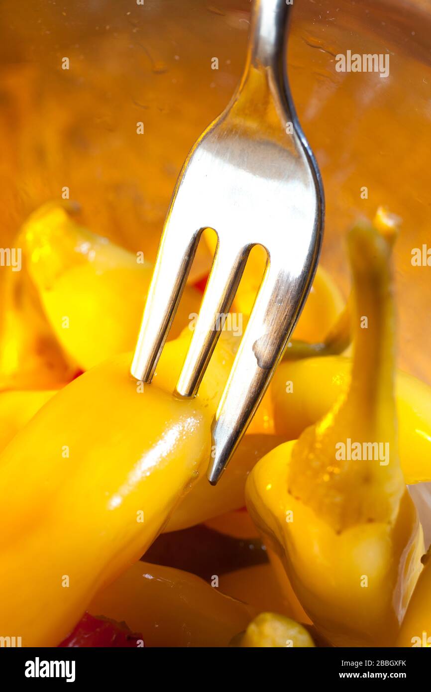 studio shot of yellow pepperoni with glittering fork in oval glass bowl ...
