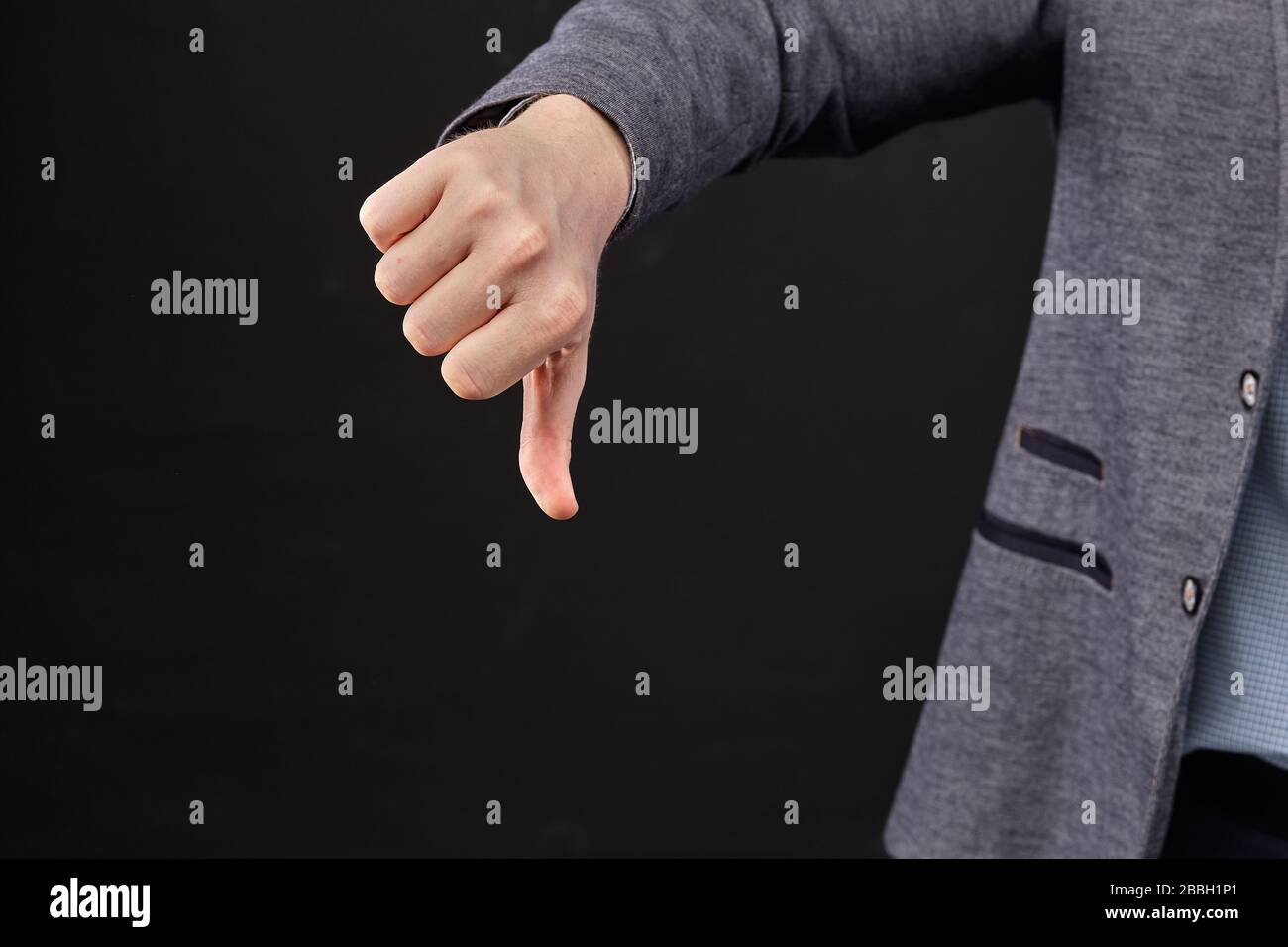 A hand in a jacket shows a thumb down as a symbol of dislike. Close up ...