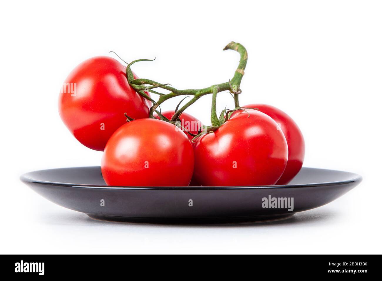 five tomatoes on a branch on a black plate isolated on white background ...