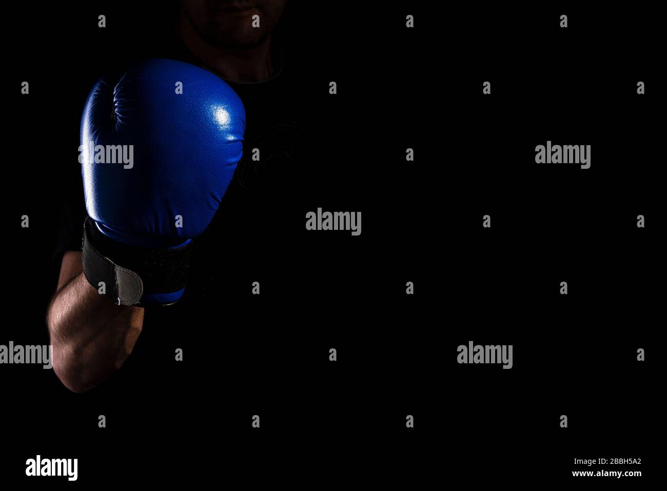 Men's hand in a blue boxing glove on a black background makes a punch ...