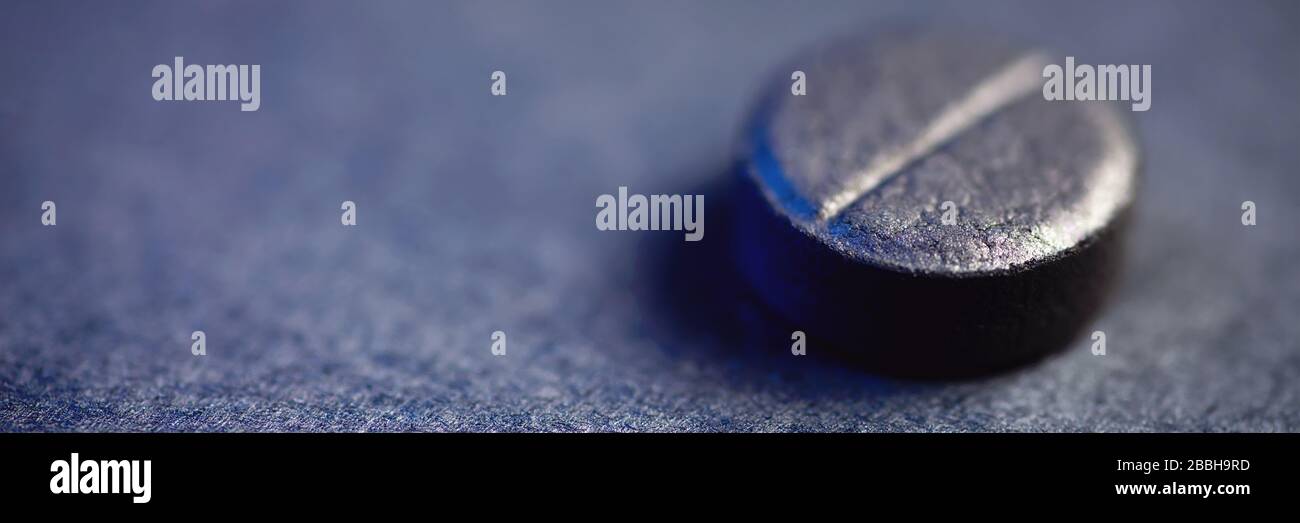 The black activated charcoal tablet. On a dark background. There's blue ...