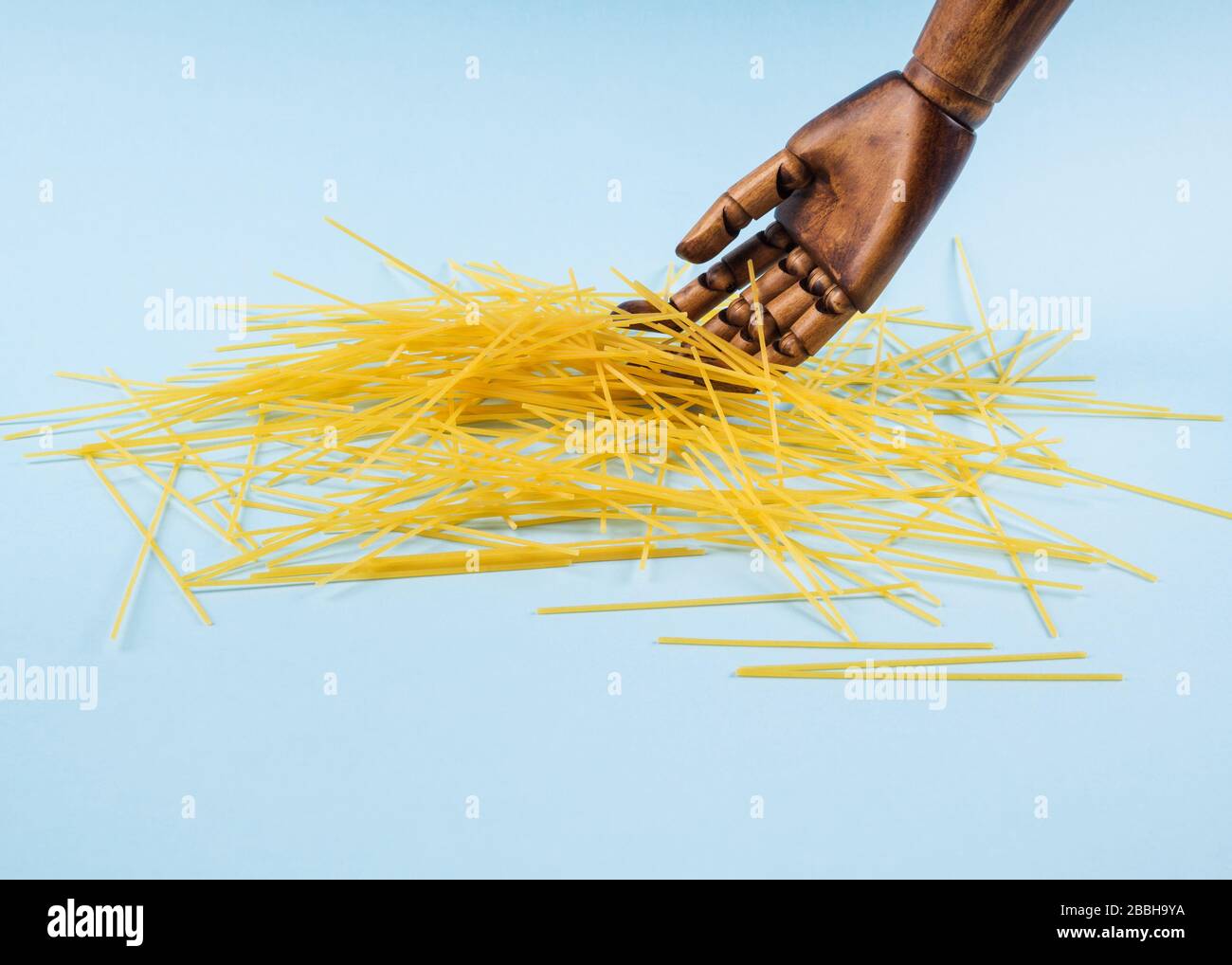 Broken spaghetti on blue with wooden hand Stock Photo - Alamy