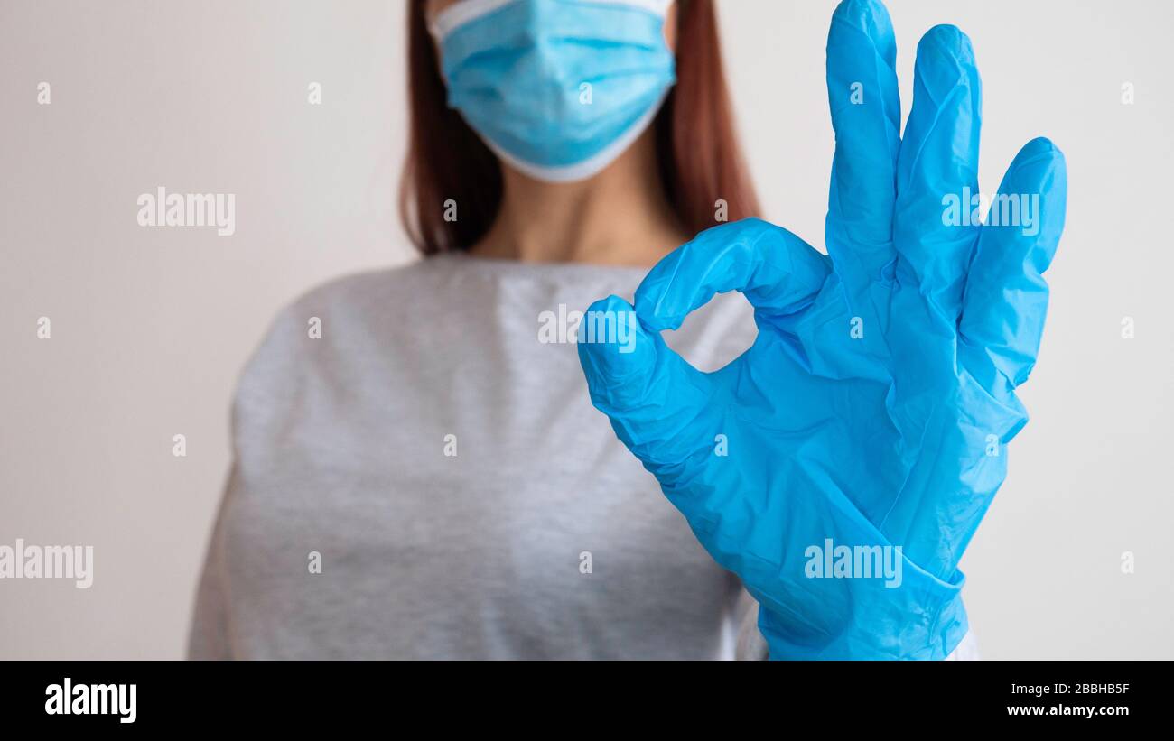 Woman with a surgical mask shows by hands in latex glove a symbol OK ...