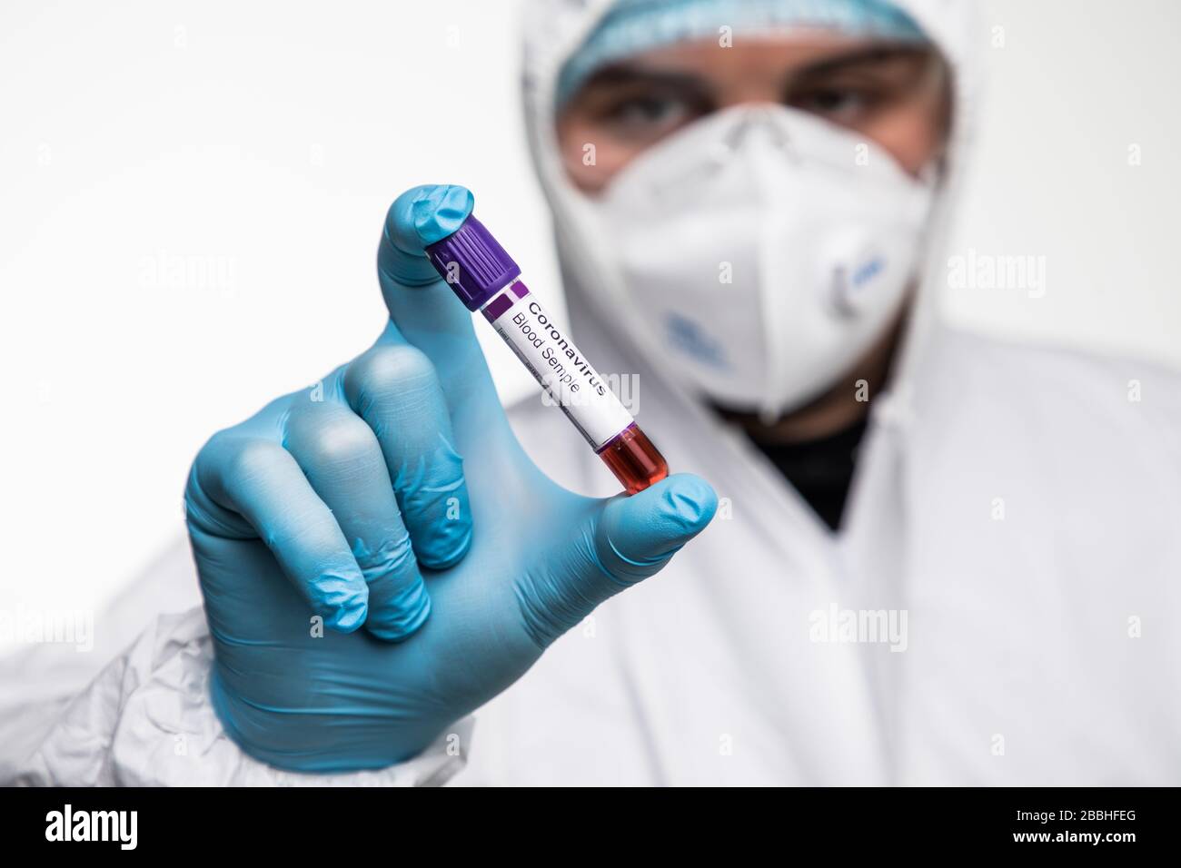 Medic man wearing HAZMAT protective clothing holding test tube filled ...