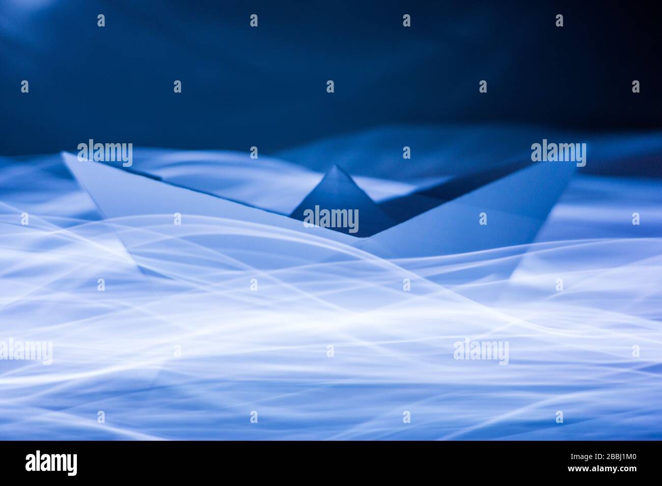 Paper boat splitting blue light trails symbolizing waves in the sea ...