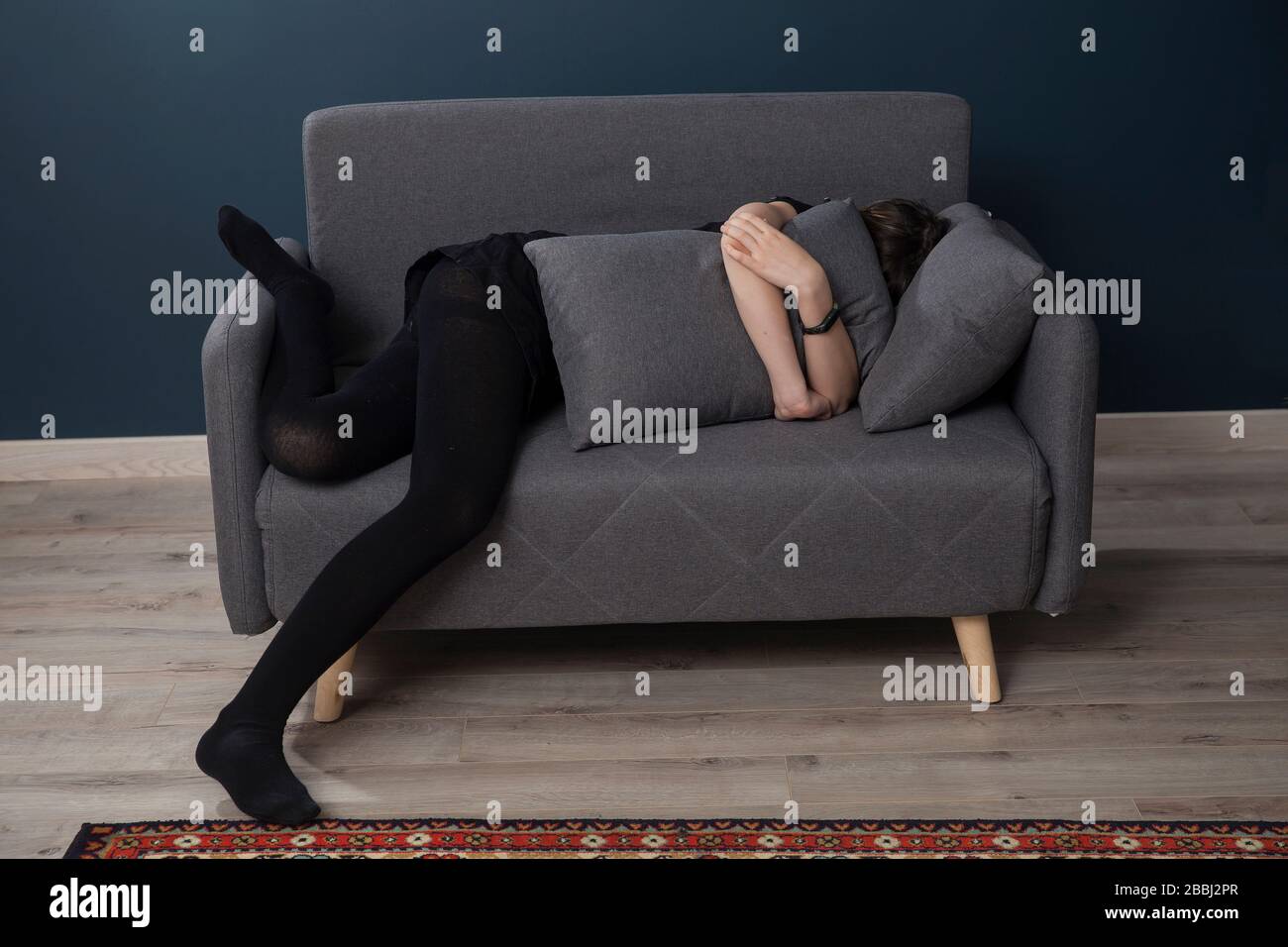 Sad girl in black tights cries, hugging a gray pillow, lying on a sofa ...
