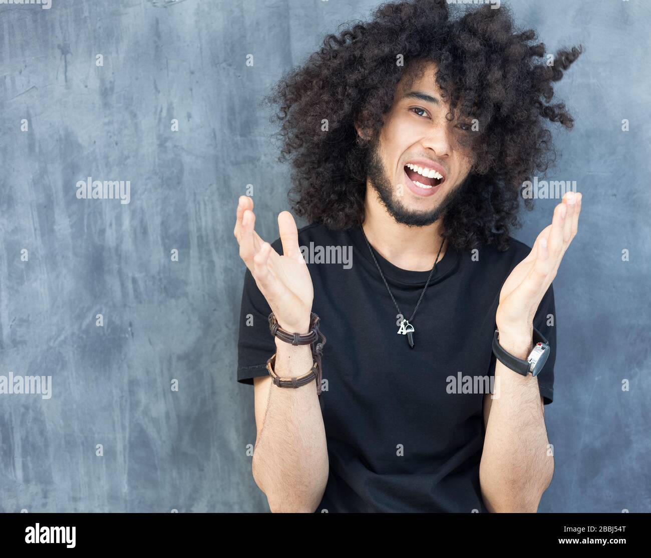 A young man with an afro hairstyle and a beard is laughing and clapping ...