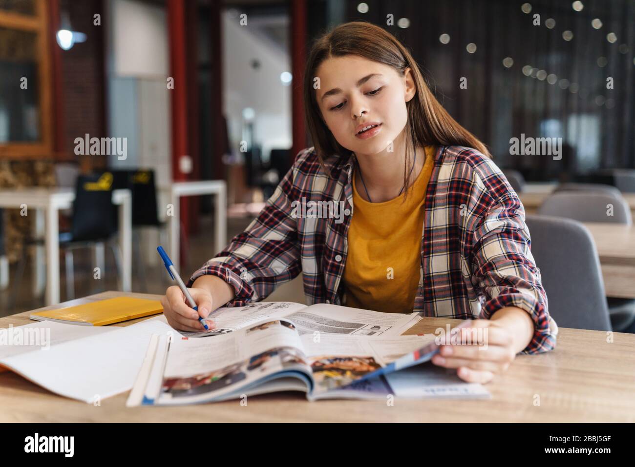 Image of serious caucasian girl doing homework with exercise books ...