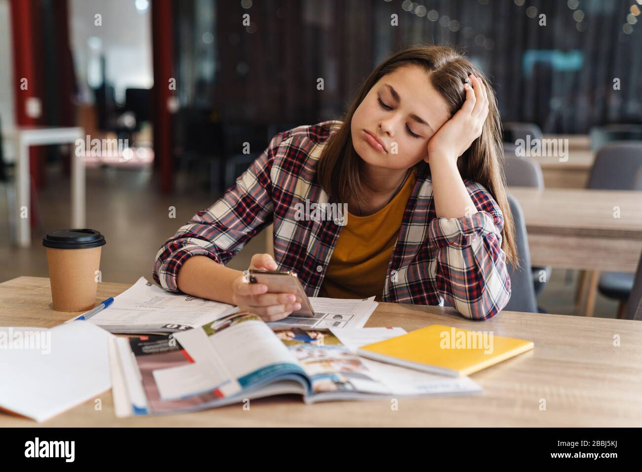 Image of sad caucasian girl using cellphone while doing homework with ...