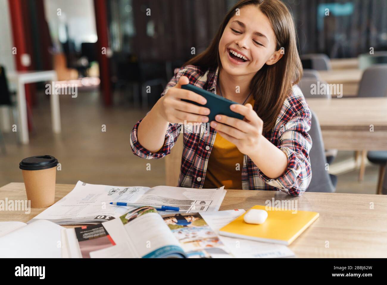 Image of joyful cute girl playing video game on cellphone while doing ...