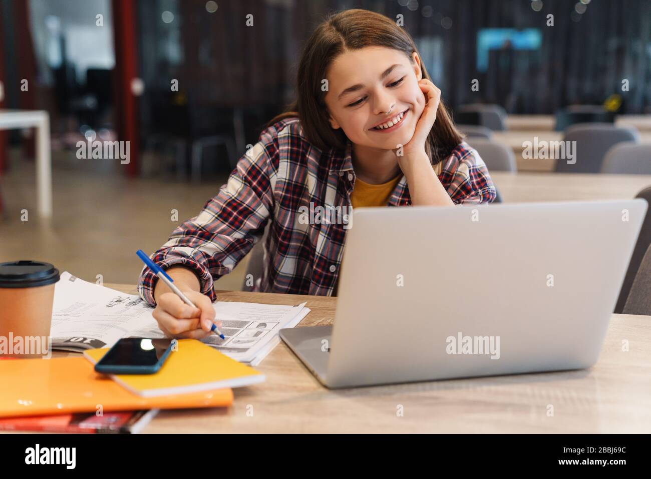Image of smiling girl doing homework with laptop and exercise books ...