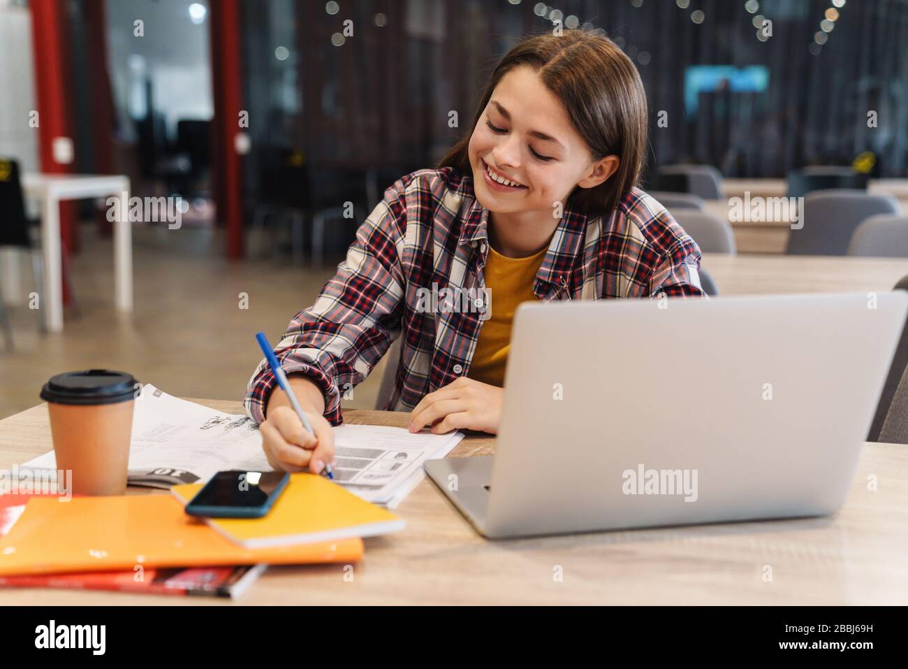 Image of smiling girl doing homework with laptop and exercise books ...