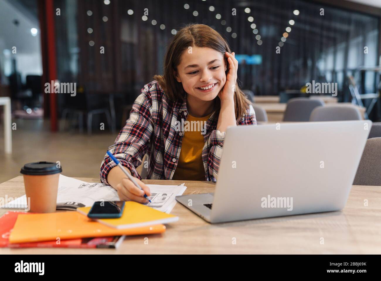 Image of smiling girl doing homework with laptop and exercise books ...