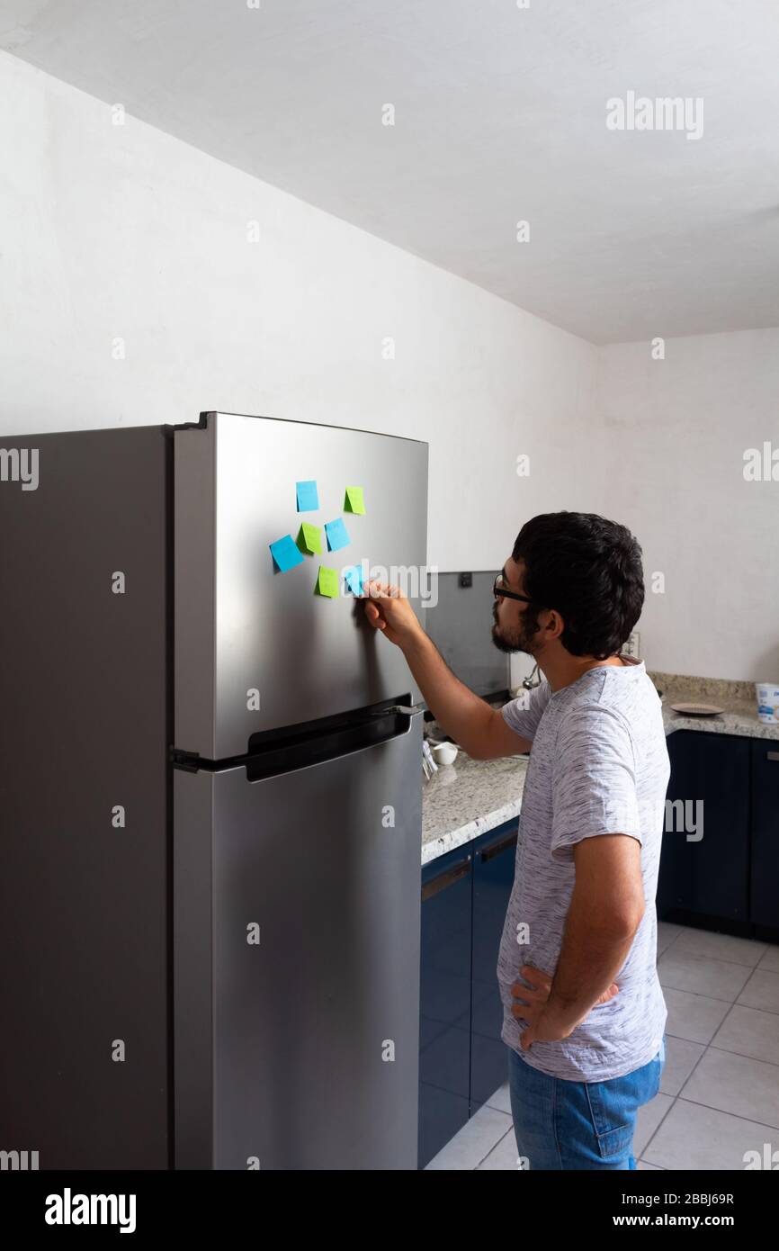 Hispanic young man taking and reading sticky posticks in his fridge ...