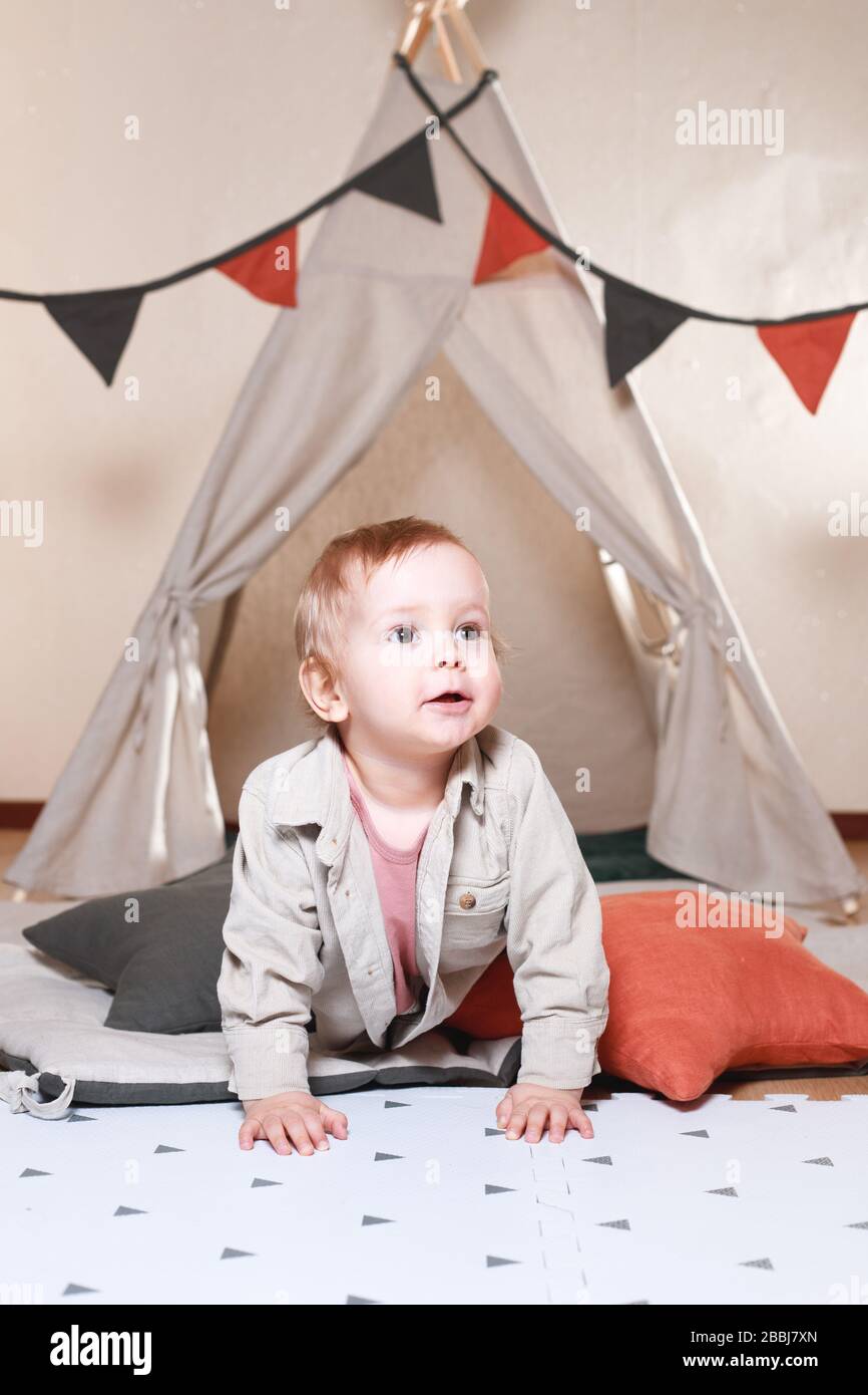 A child, a boy, is sitting and playing in a tent inside the house on a ...