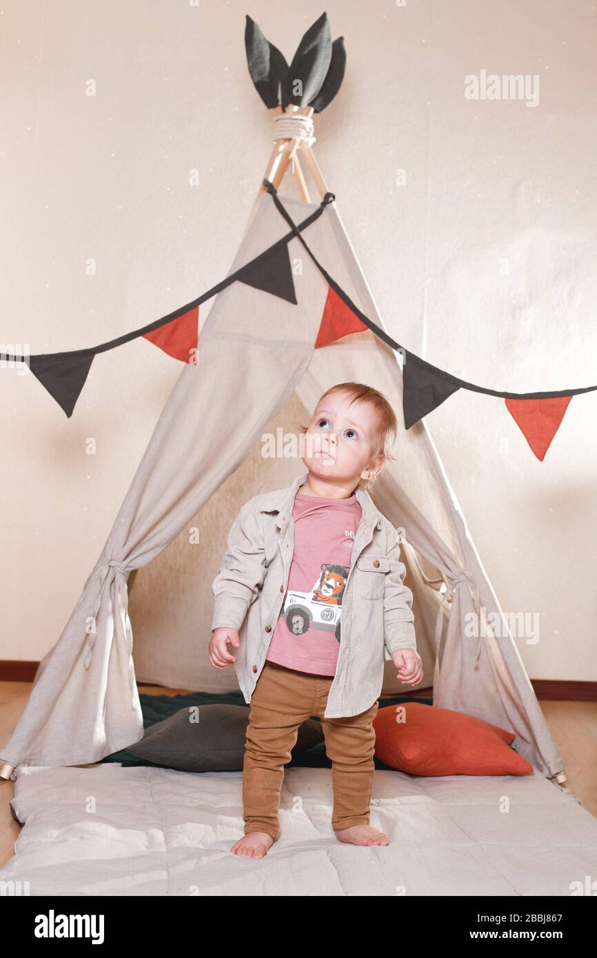 A child, a boy, is sitting and playing in a tent inside the house on a ...