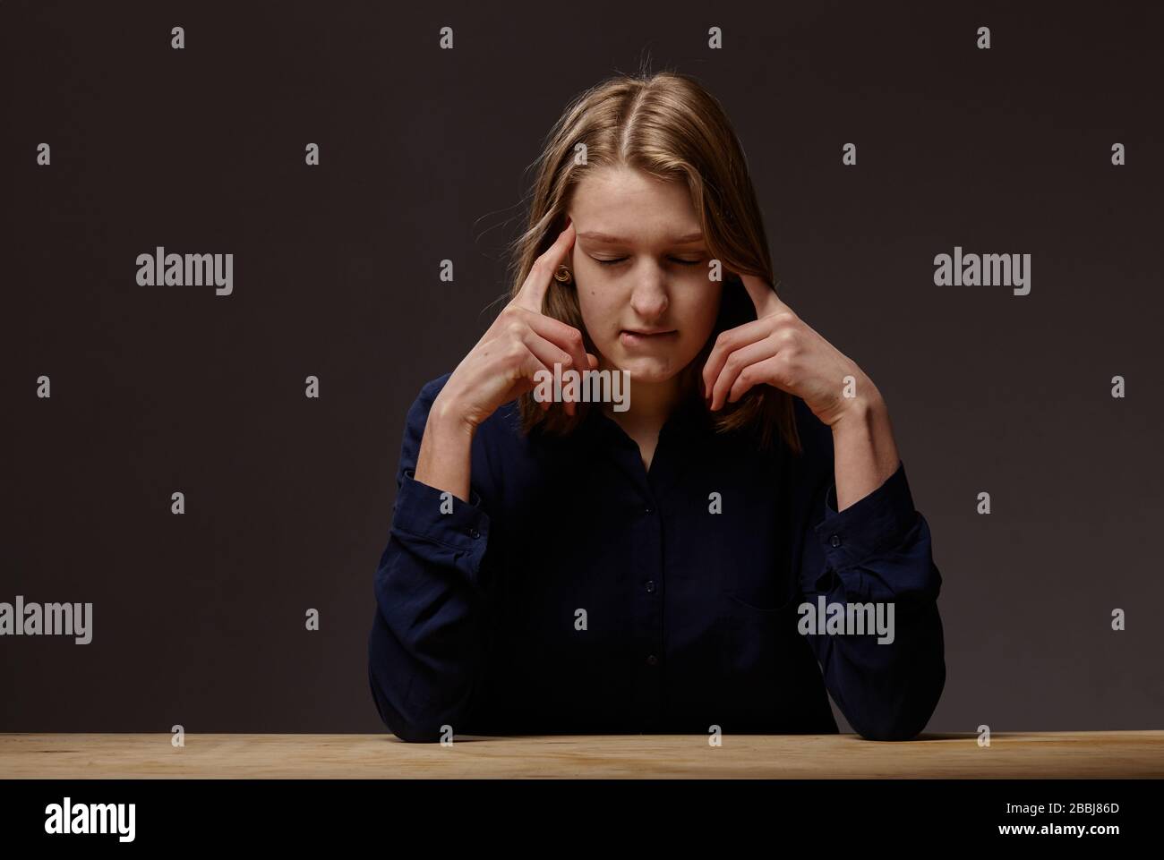 very tense young woman at the table on a dark background Stock Photo ...