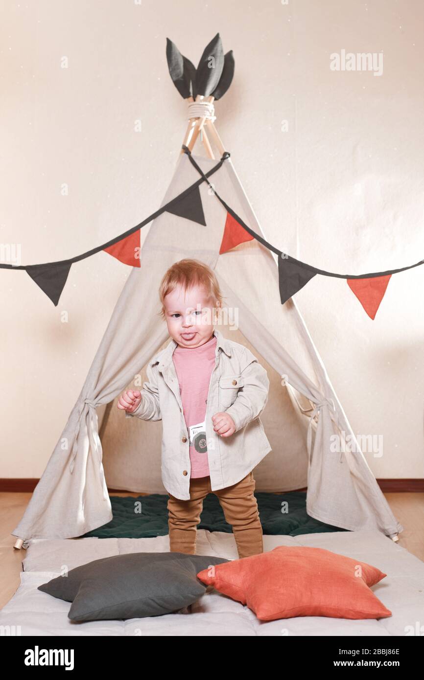 A child, a boy, is sitting and playing in a tent inside the house on a ...