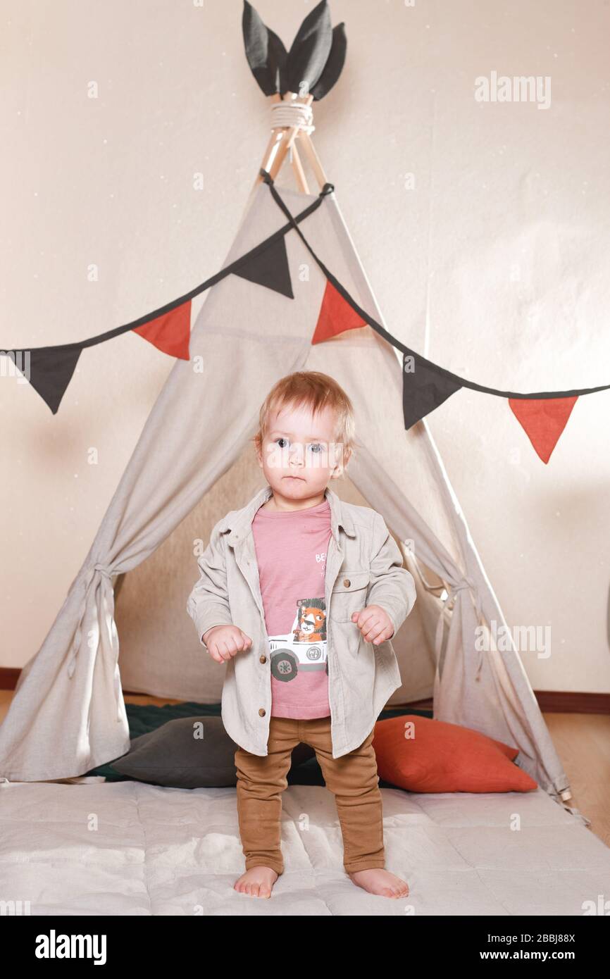 A child, a boy, is sitting and playing in a tent inside the house on a ...