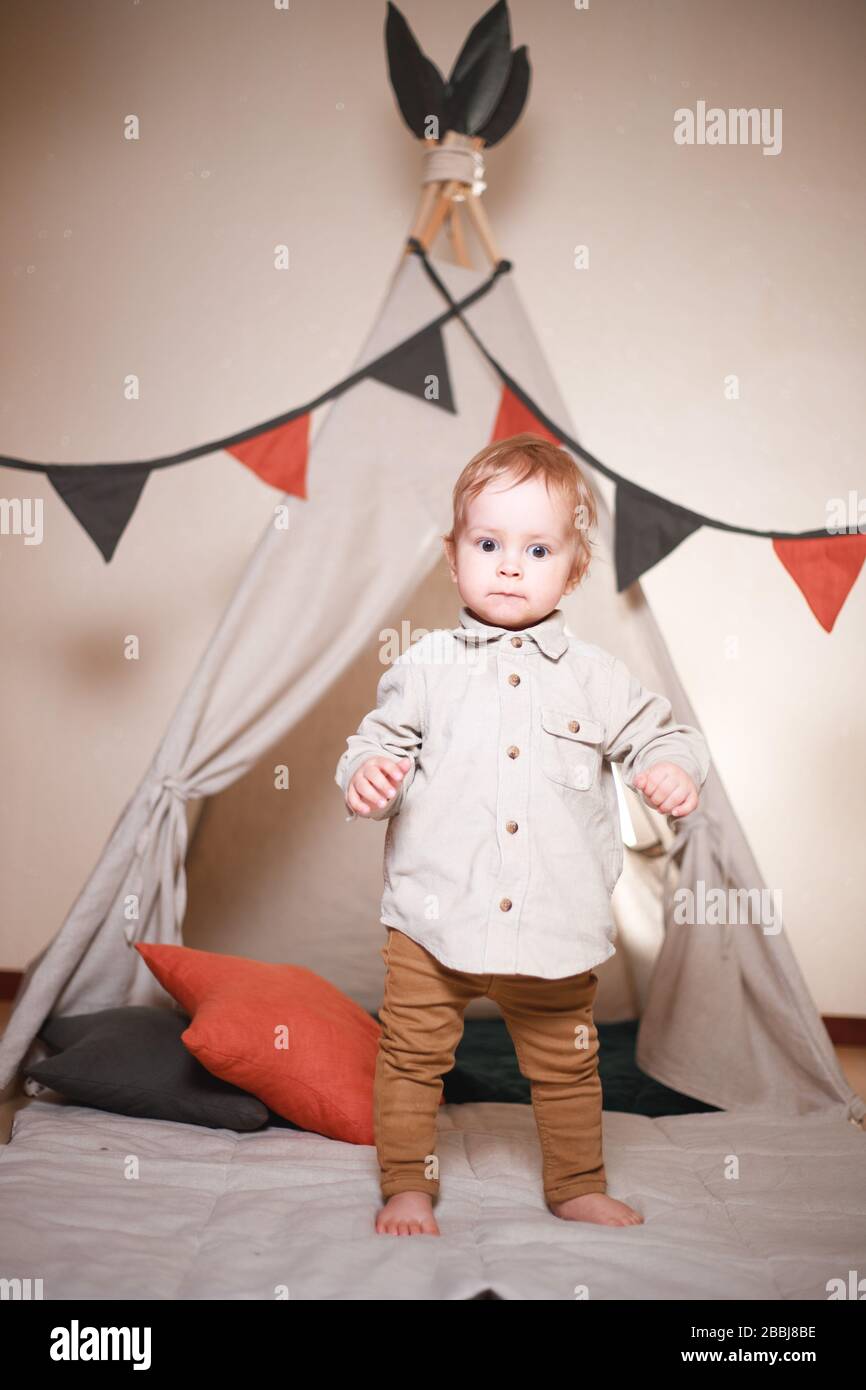 A child, a boy, is sitting and playing in a tent inside the house on a ...