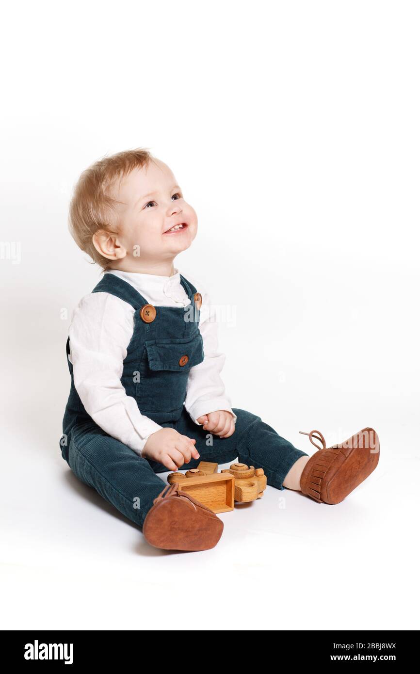 a cute one-year-old child stands in a White Studio. The boy has a happy ...