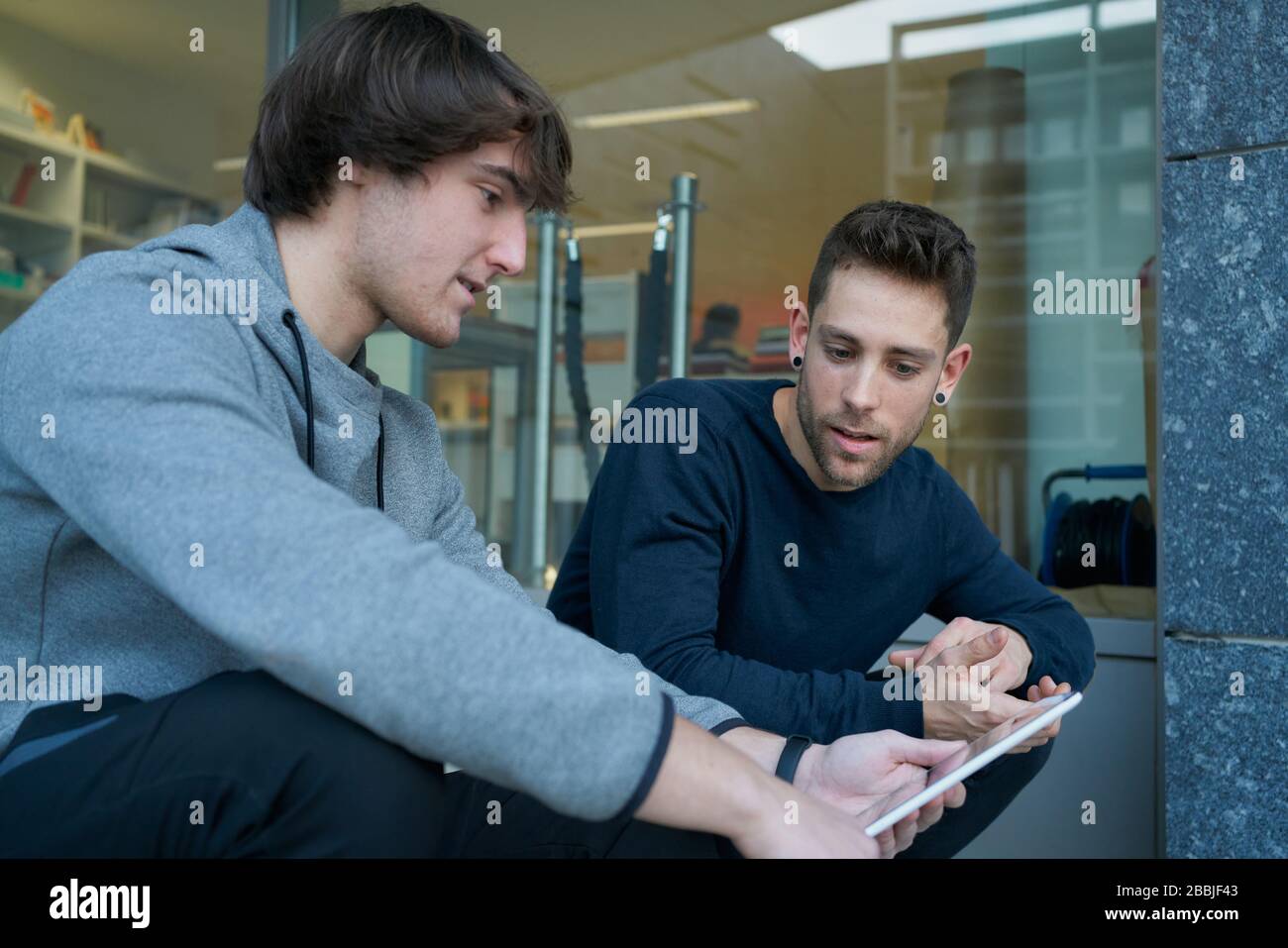Front view of two young men talking sitting on a city staircase and lo ...