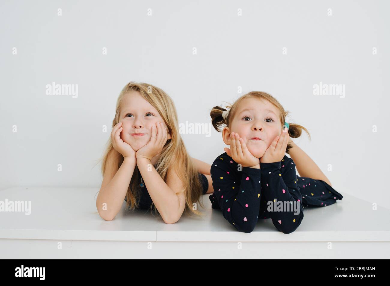 Adorable siblings lying on a table with their feet up. Over white wall ...