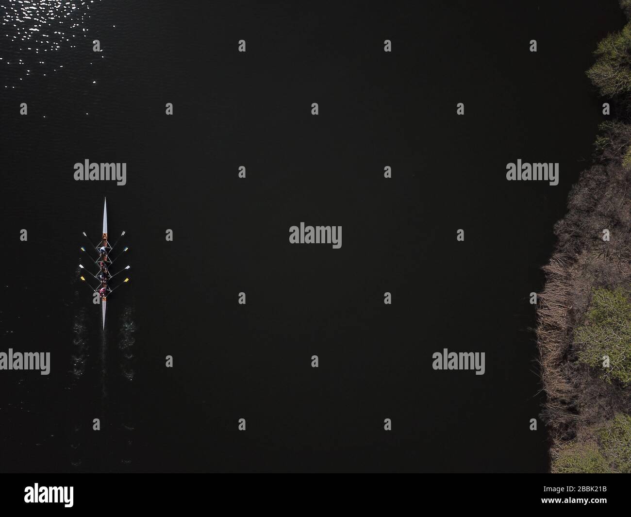 Four people rowing with an instructor in the background of black water ...