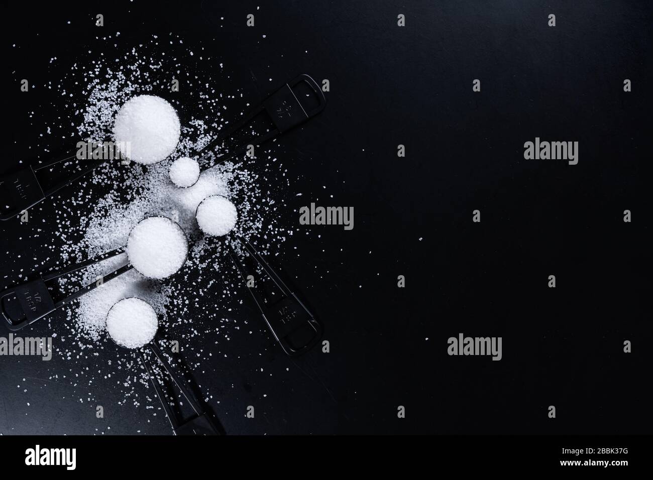 Black measuring spoons with salt on black background Stock Photo - Alamy
