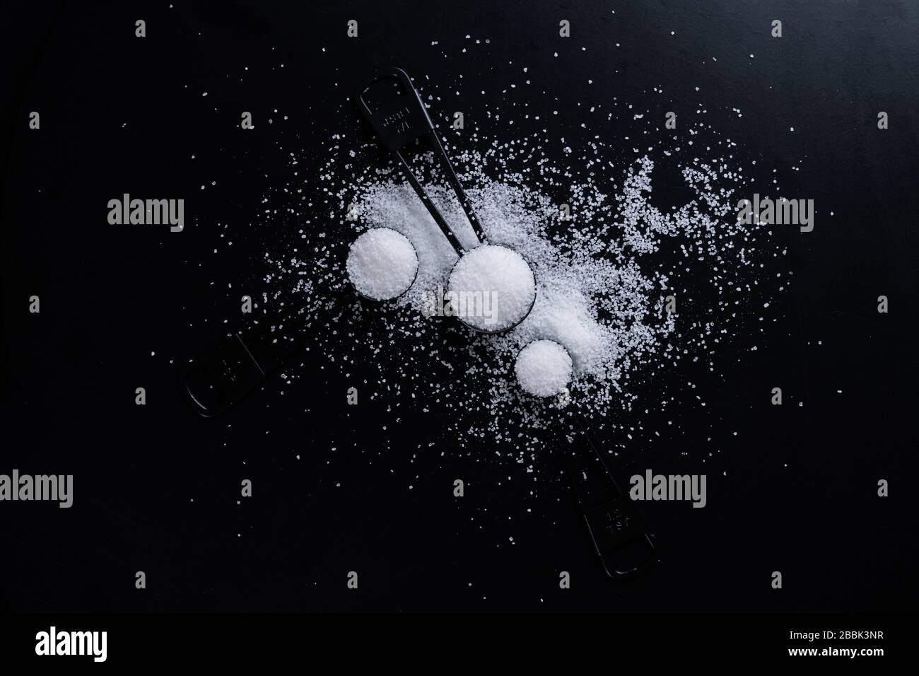 Black measuring spoons with salt on black background Stock Photo - Alamy