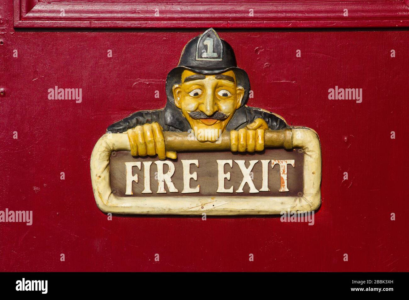 A wooden fire exit sign with a cartoon fireman hanging on a red door ...
