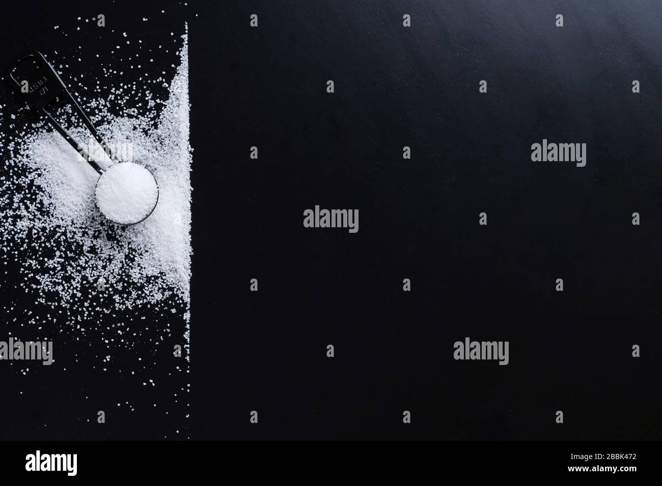 Black measuring spoons with salt on black background Stock Photo - Alamy