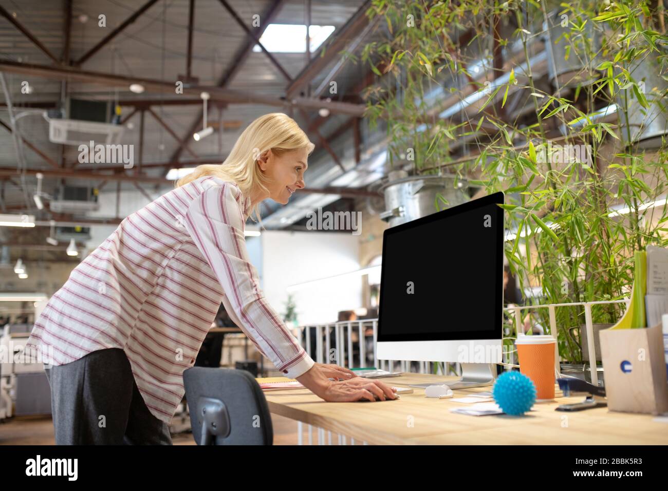 Blonde woman bending over desk, looking at screen Stock Photo - Alamy