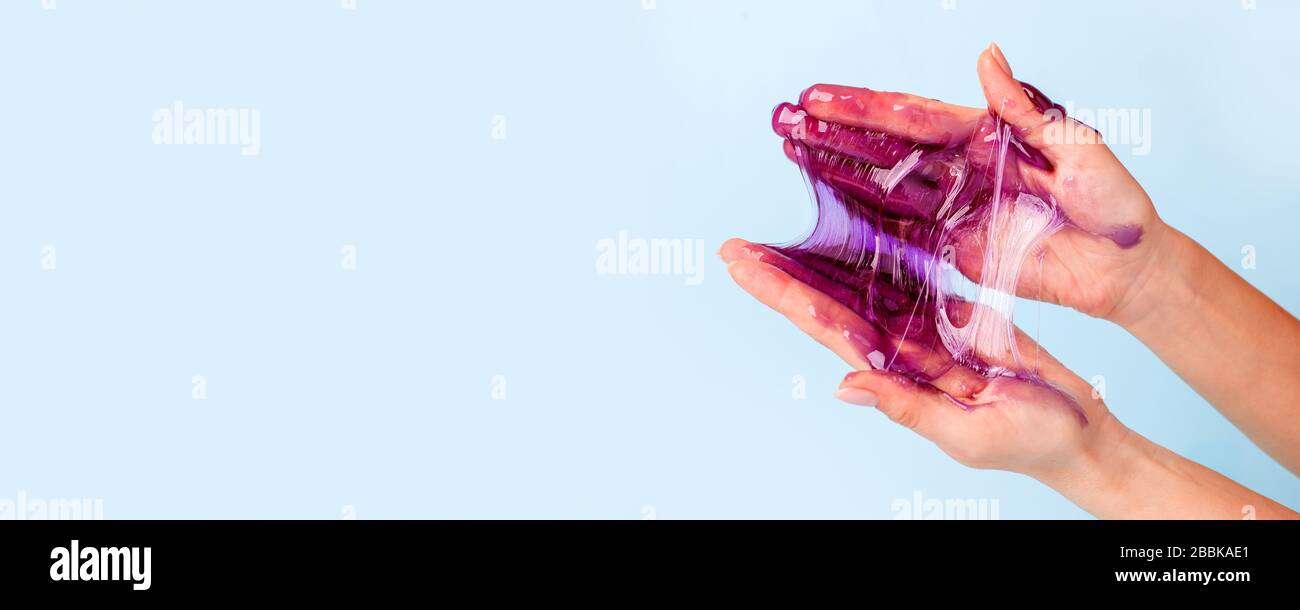 Young girl hands with sticky purple slime on blue background, liqiud ...