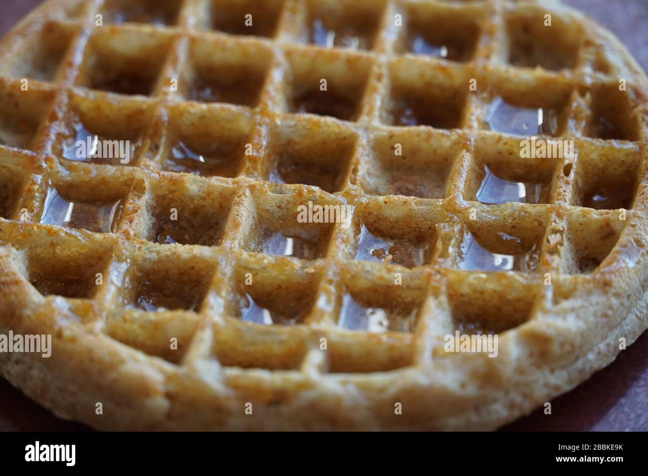 Close-up of one golden waffle with syrup in the indentations reflecting ...